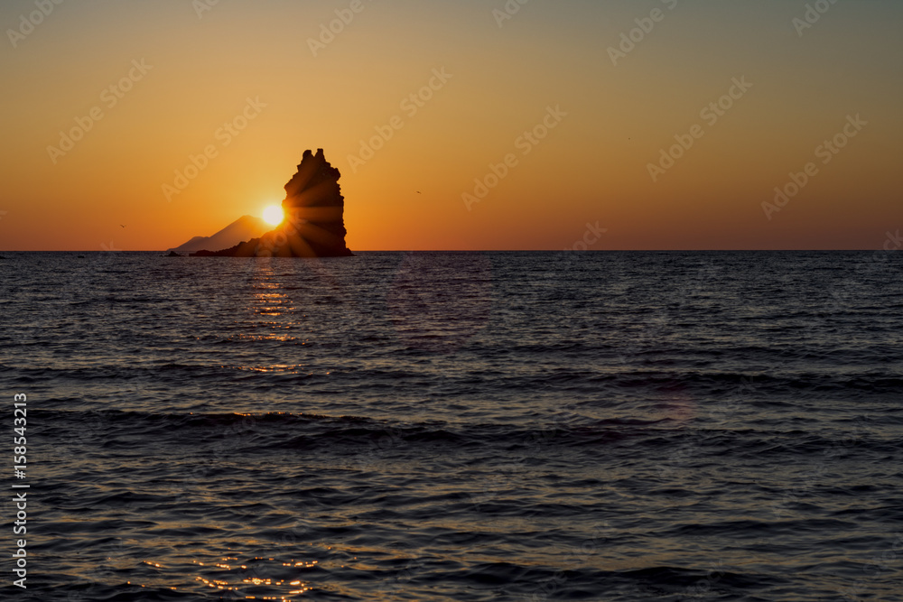 Sole che tramonta dietro al faraglione ed isola di Filicudi, arcipelago ...