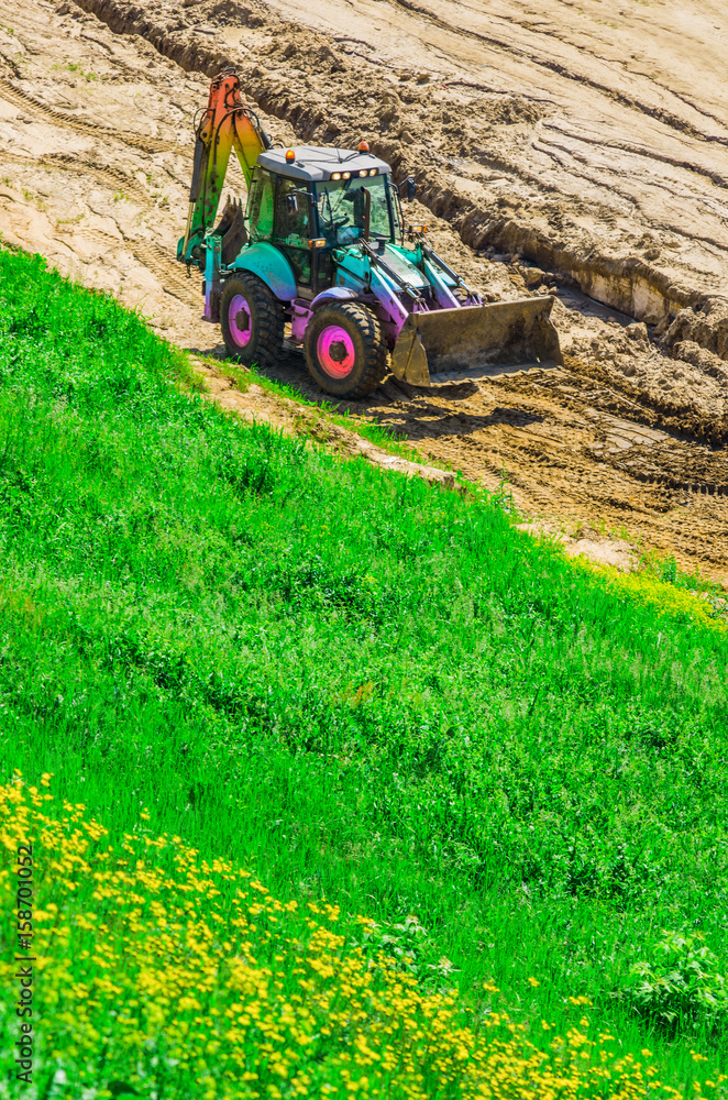 Rainbow multi-colored tractor with a bucket on a background of green ...