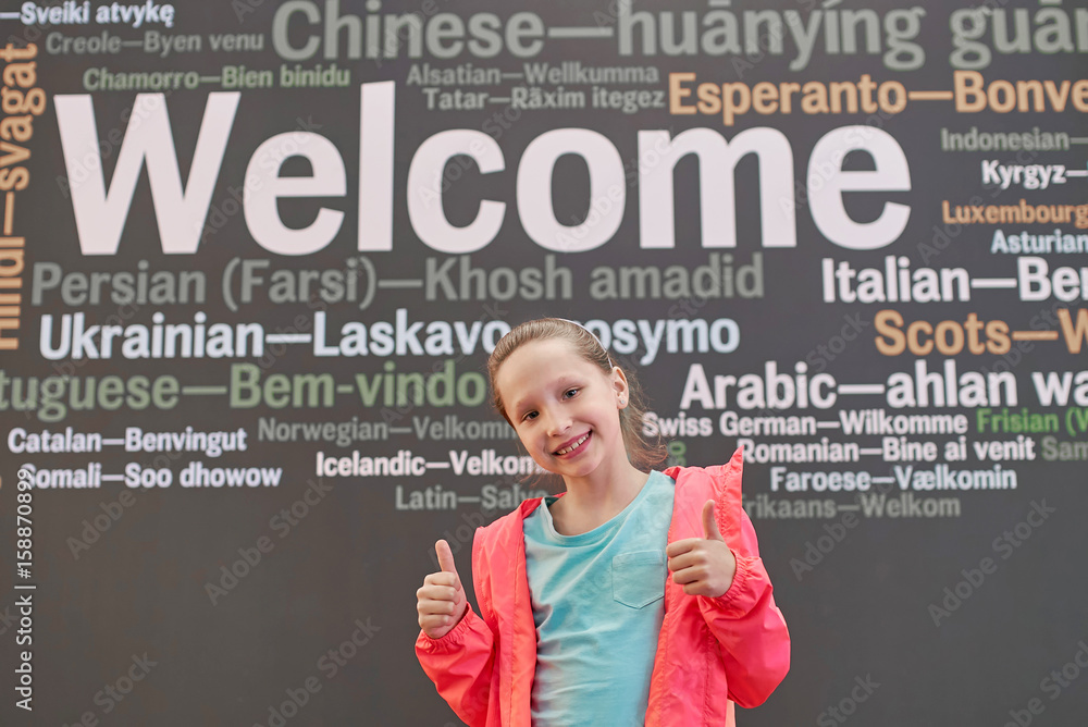 Smiling little girl in front of welcome board gesturing thumbs up, with ...