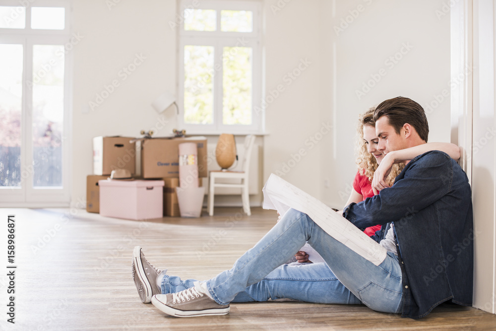 Young couple in new home sitting on floor looking at ground plan Stock ...