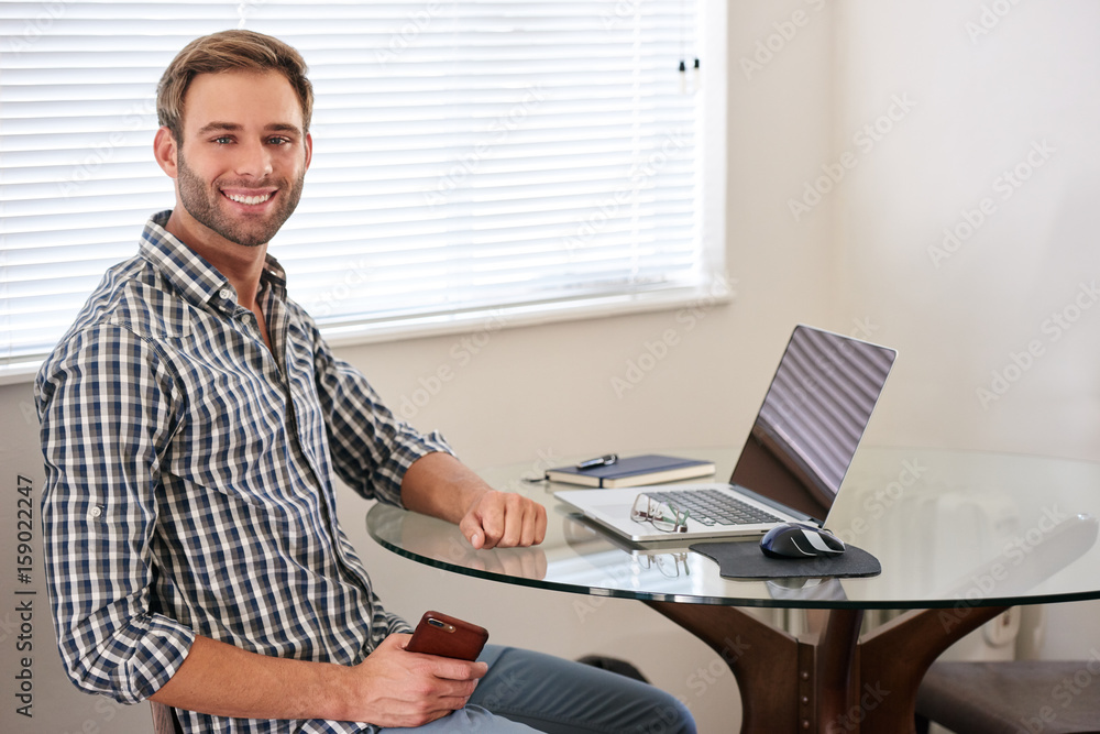 Handsome young white man sitting indoors in his house at his glass desk ...
