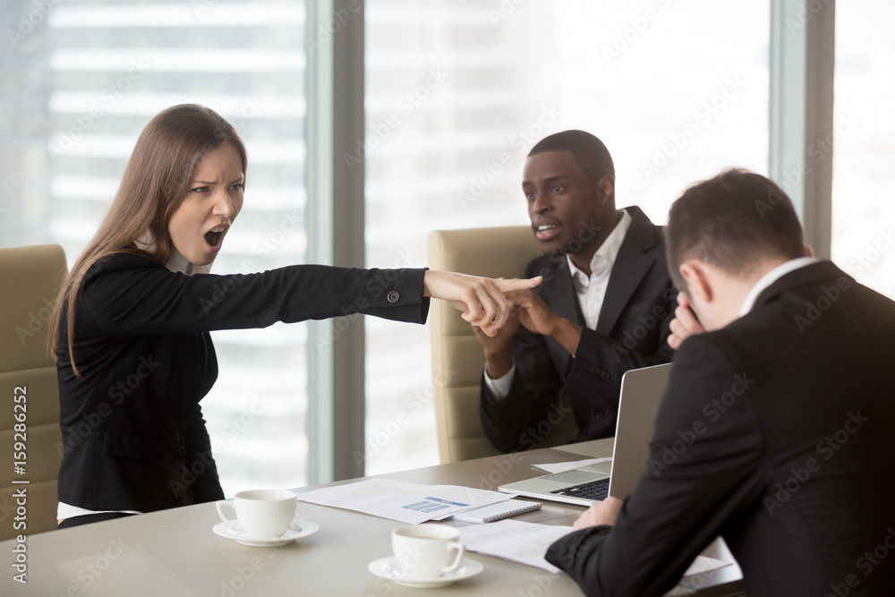 Angry female furious boss scolding employee at mixed-race team meeting ...