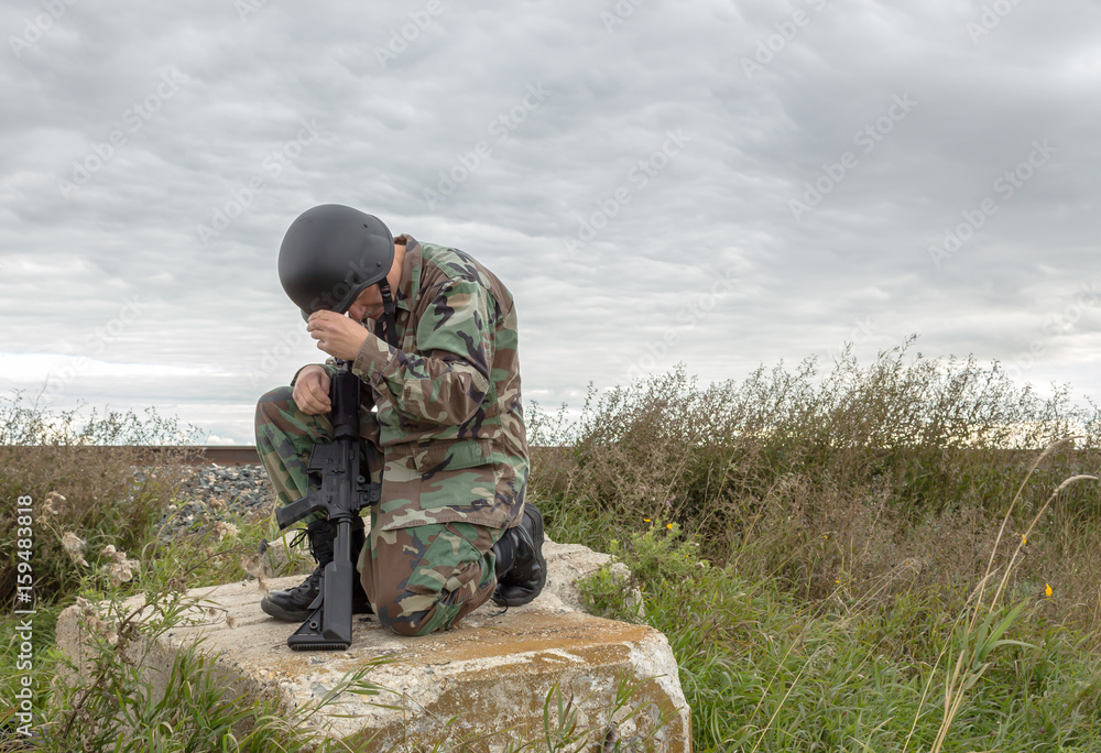 horizontal image of a soldier kneeling down on a big boulder with his ...