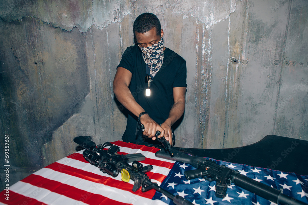 Black gun dealer checks a weapon. Mercenary man with gun in hand on ...