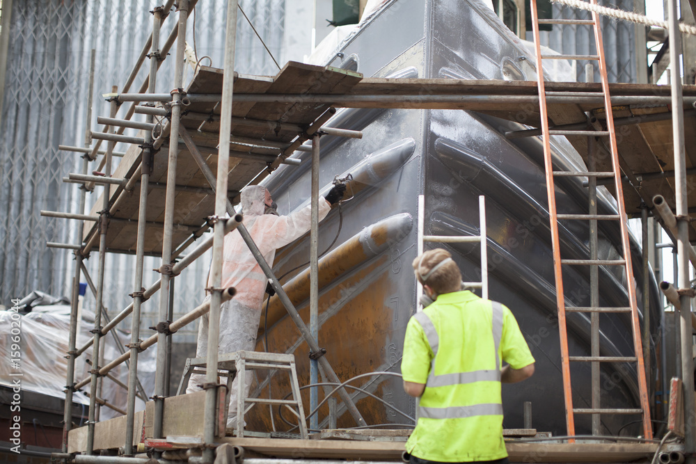Workers spray-painting boat hull in shipyard Stock Photo | Adobe Stock