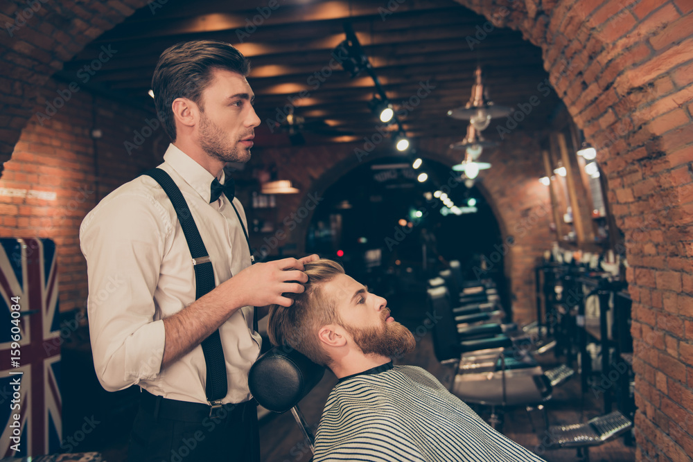 Barber shop classy dressed specialist is styling the hair of a client ...