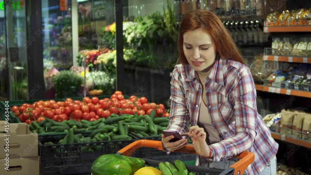 Pretty young woman browsing her shopping list on her smartphone at the ...