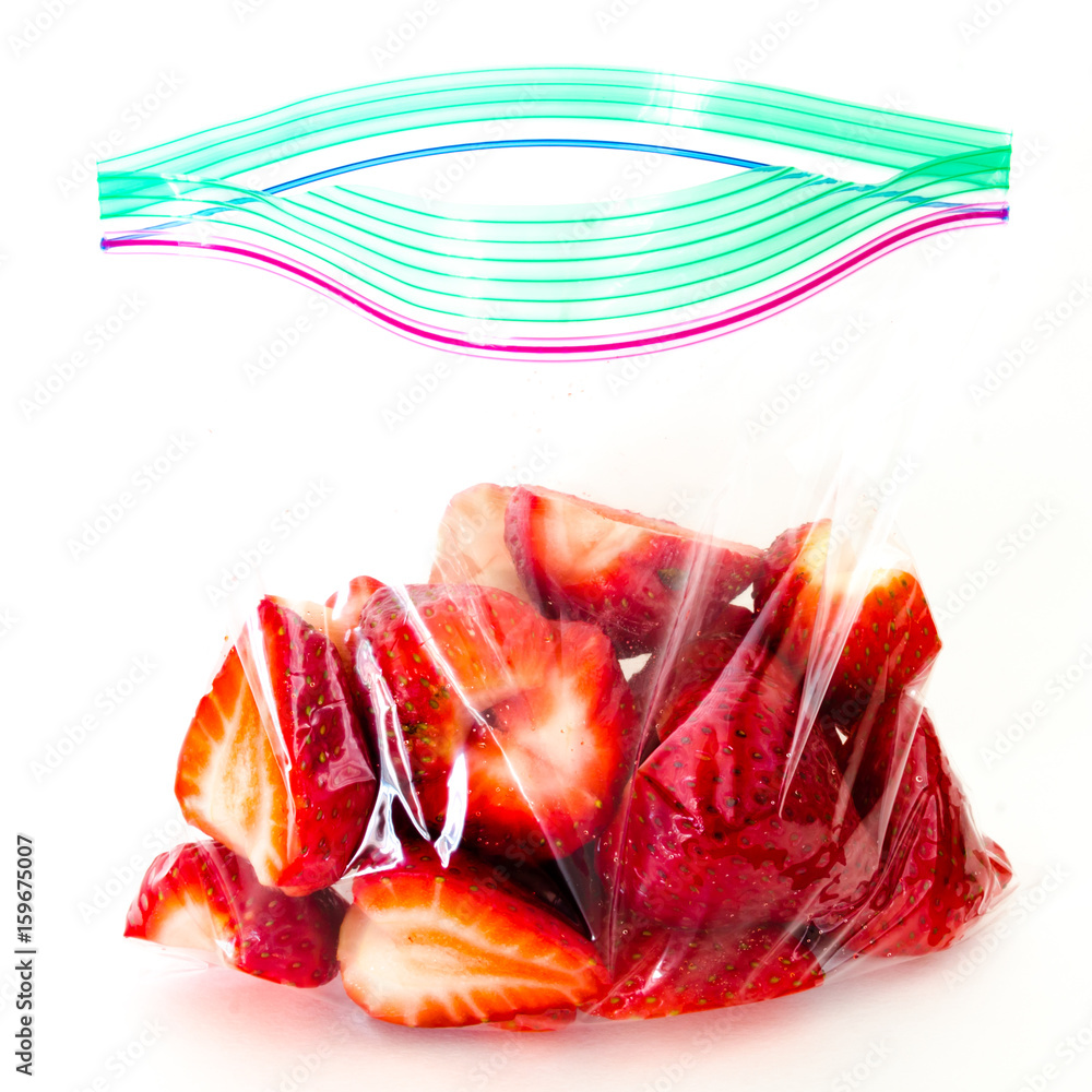 Studio shot fresh chopped strawberries in clear open plastic bag with ...