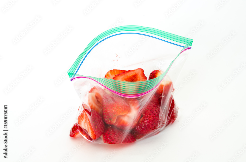 Studio shot fresh chopped strawberries in clear open plastic bag with ...
