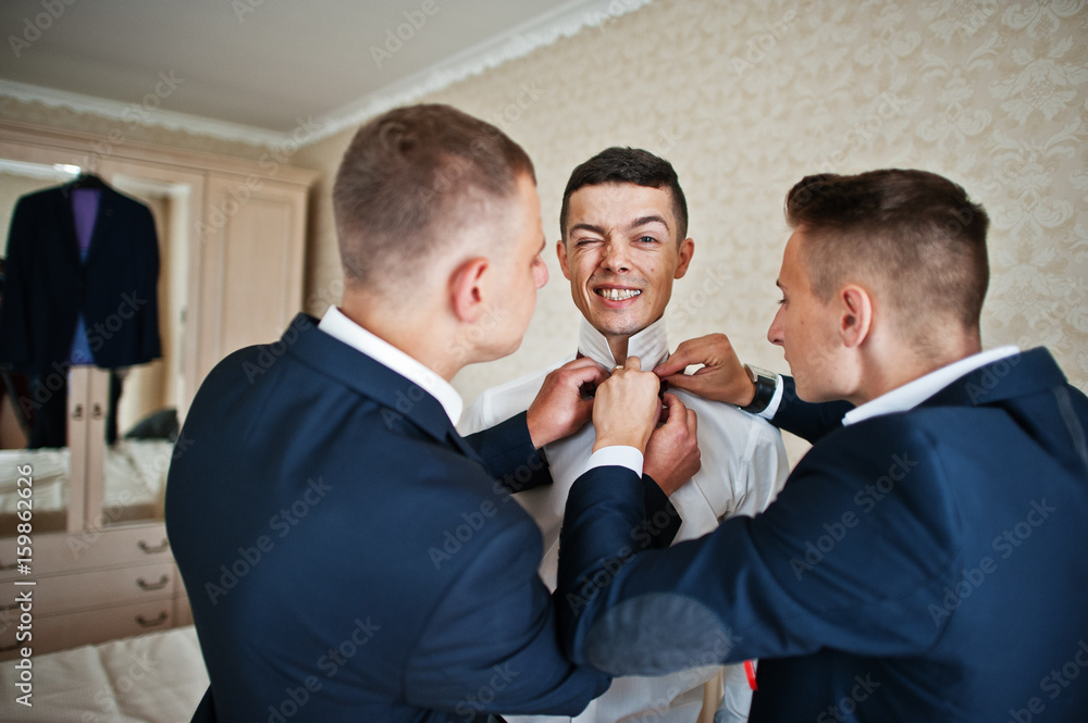 Groomsmen helping groom to dress up and get ready for his wedding in a ...