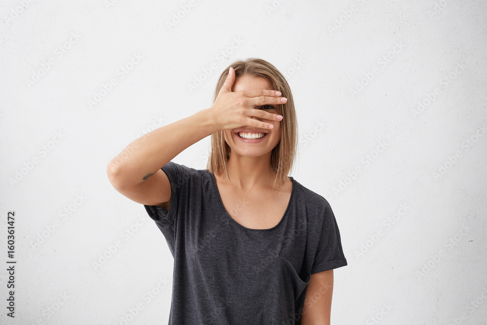 Merry woman having shy look peeking through her fingers demonstrating ...