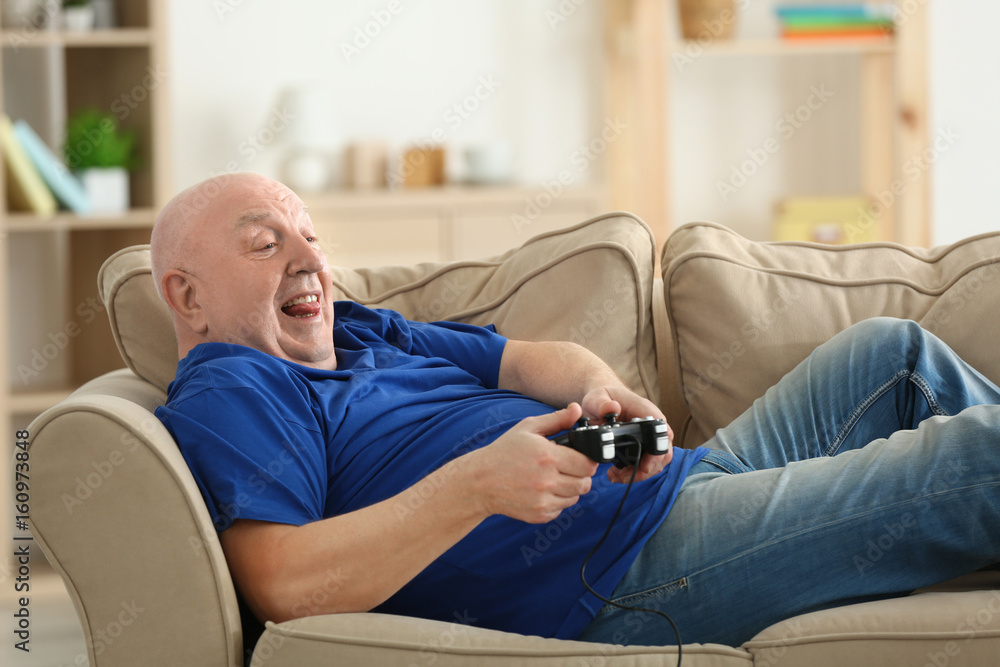 Fat senior man playing videogame while lying on sofa at home. Sedentary ...