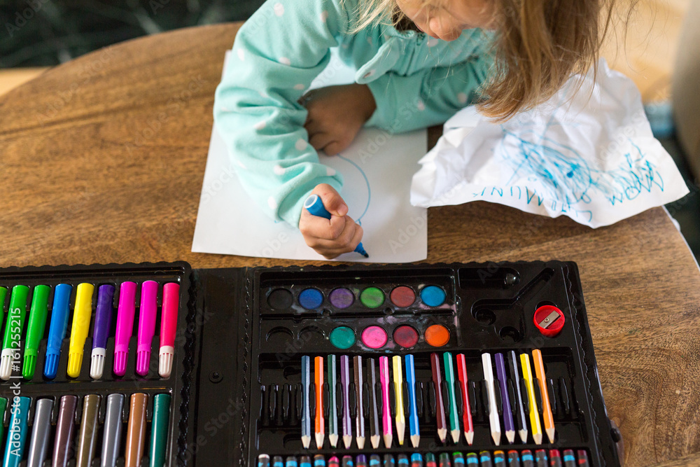 Young girl at home, drawing on white paper, art kit in front of her ...