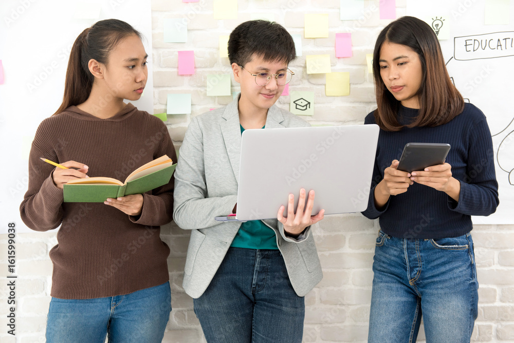 Students standing by the wall in classroom looking at laptop computer ...