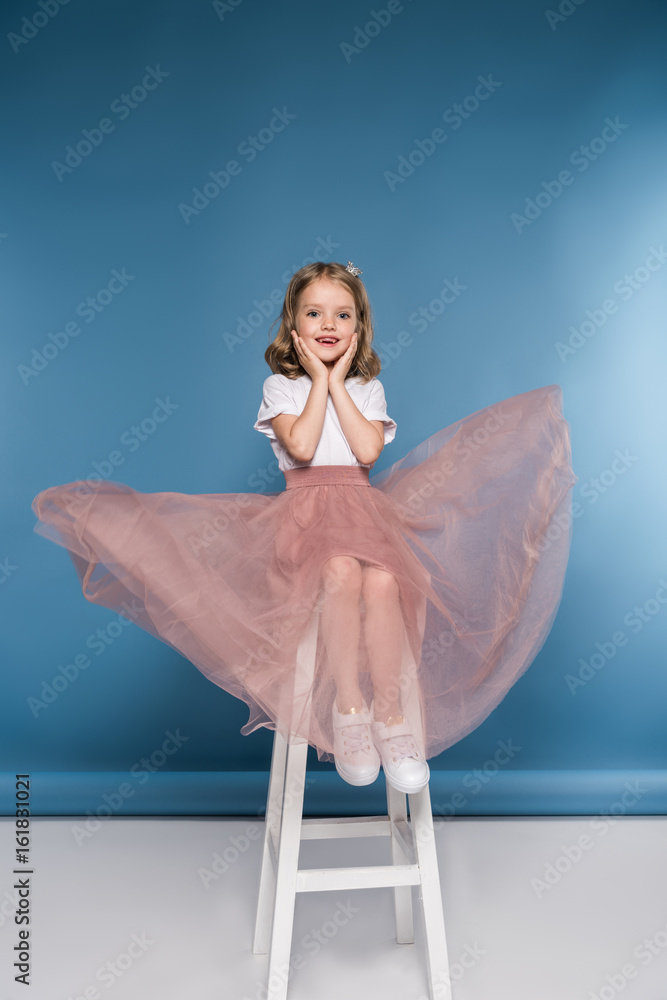 Adorable little girl in pink skirt sitting on ladder and looking at ...
