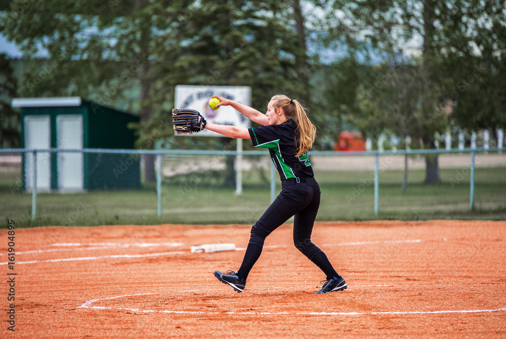 A teenage girl in fast ball pitching stance on the pitchers mound in ...