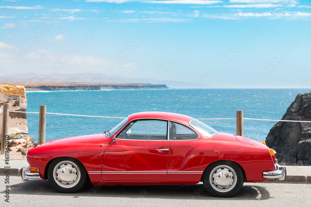 Old red car parked on a side of a road with blue ocean and sky in the ...