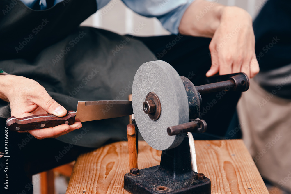 master sharpens the knife by tradition on a hand grindstone. Concept is ...
