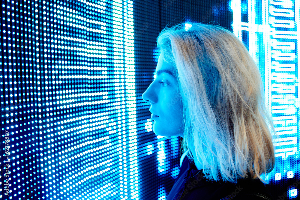 The concept of a digital future. Young blonde girl looking at the led ...
