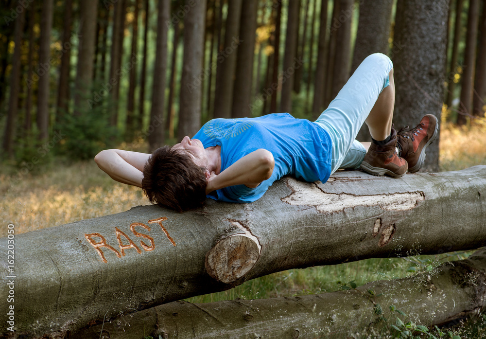 Frau liegt entspannt auf Baumstamm in den das Wort Rast eingeritzt ist ...
