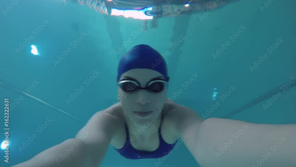 Female athlete in cap and goggles holding camera and swimming ...