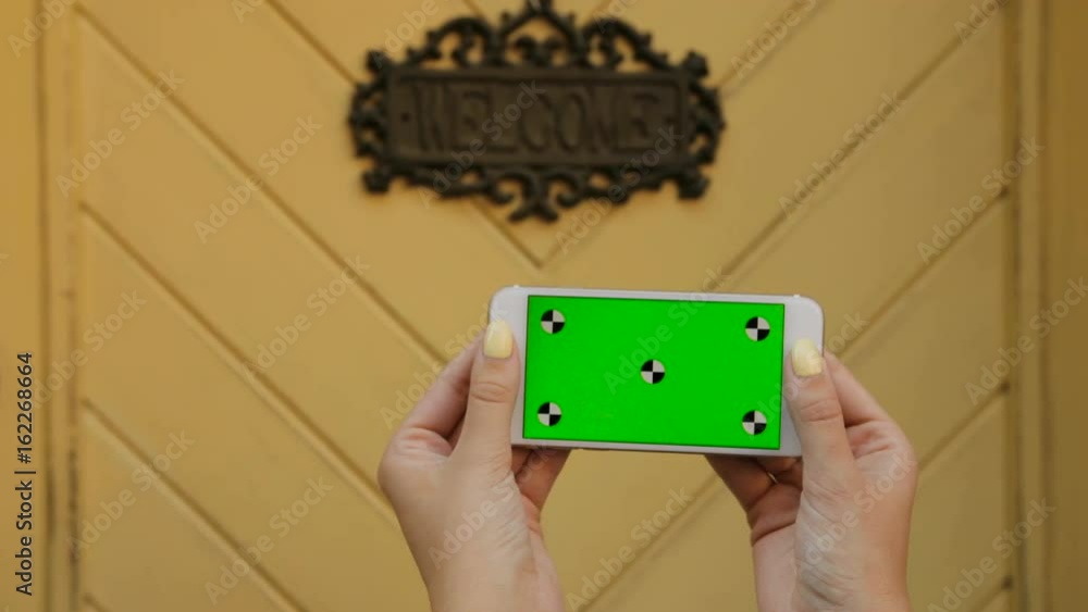 Woman holding white smartphone with green screen on yellow door ...