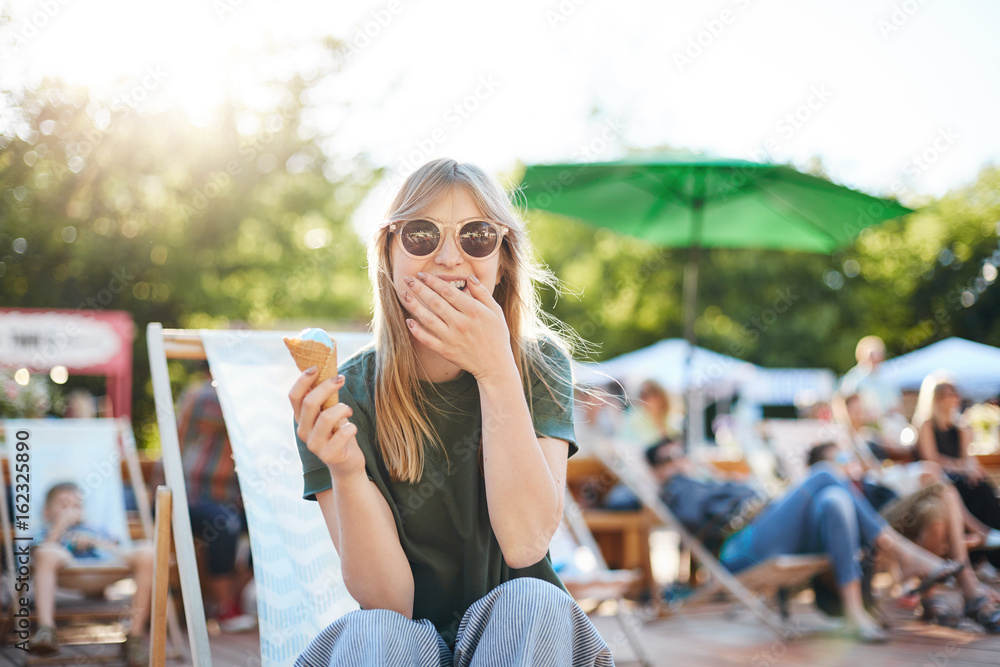 Lady eating ice cream laughing. Portrait of young female sitting in a ...