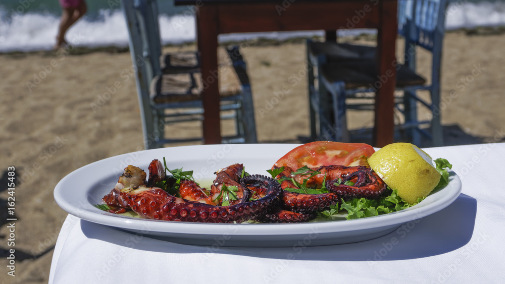 Grilled octopus with olive oil, tomato and lemon slice on a dish by the ...