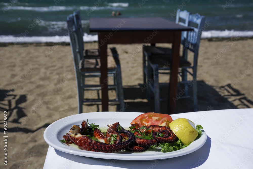 Grilled octopus with olive oil, tomato and lemon slice on a dish by the ...