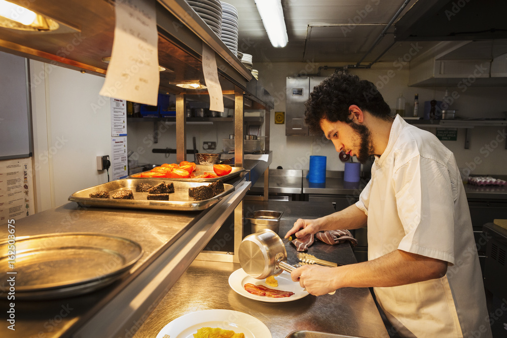 Chef standing in a restaurant kitchen at a counter, holding sauce pan ...