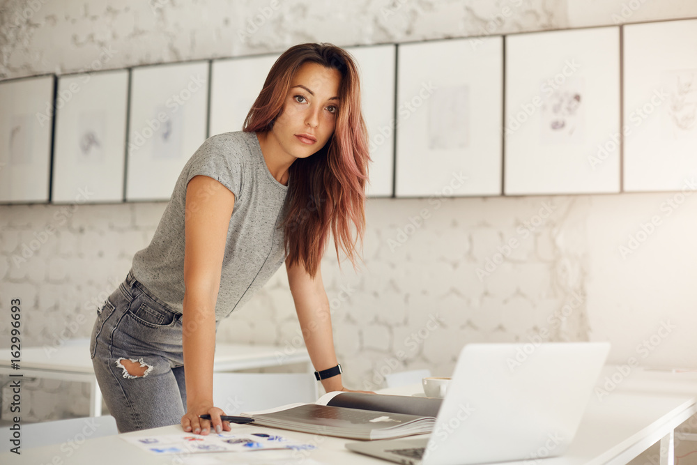Female graphic artist sketching in her studio working on laptop reading ...