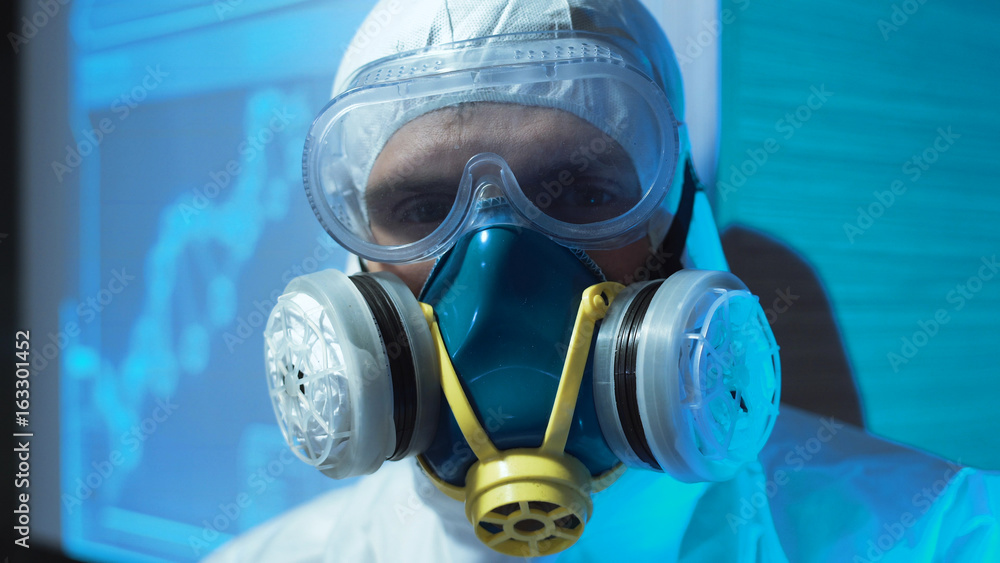 Person in a laboratory wearing a biohazard suit and mask with breathing ...