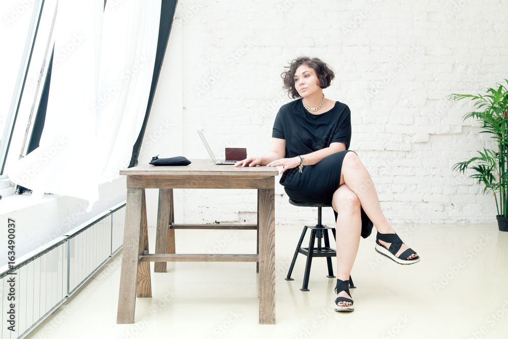 Young plus size female model sitting in front of the table and working ...