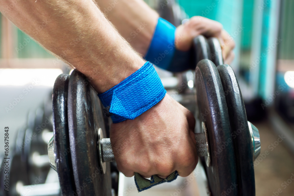 hand in palm protection grips takes Dumbbell from stand. Blurred gym in ...