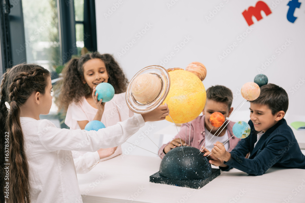 Multiethnic group of schoolchildren working with solar system model in ...
