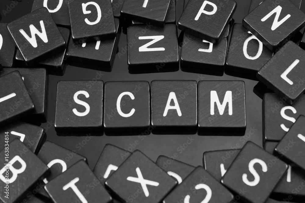 Black letter tiles spelling the word "scam" on a reflective background ...