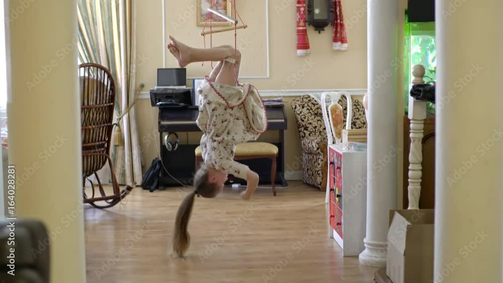 Wide shot of little girl in simple linen dress hanging upside down on ...