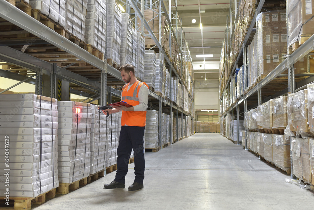 Man in factory hall wearing safety vest holding clipboard scanning ...