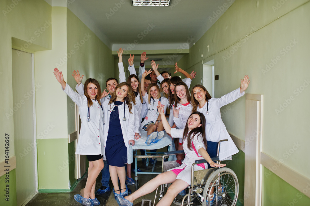 Crazy young doctors having fun by posing on a wheelchair in the hallway ...