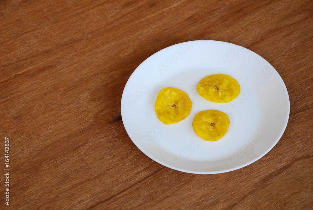 Dried and fried banana slices place on white plate isolated on wood ...