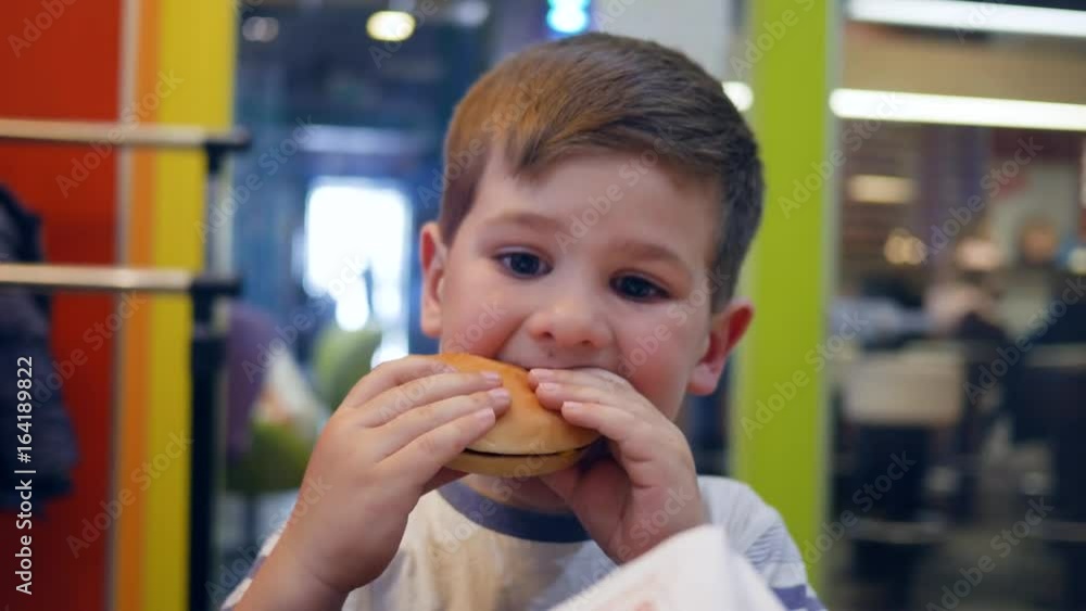 Small boy eats with appetite in childrens restaurant, child eating food ...