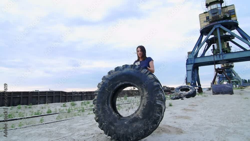 A young athletic woman performs exercises using a large heavy tractor ...