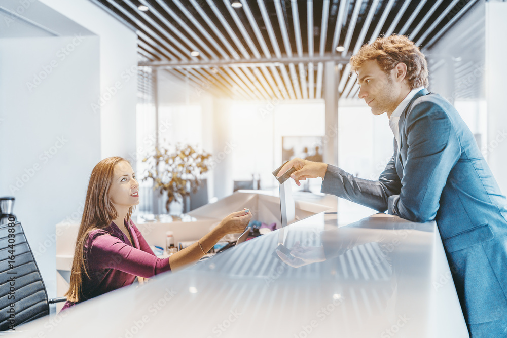 Handsome elegant caucasian man in formal suit is leaning on white table ...