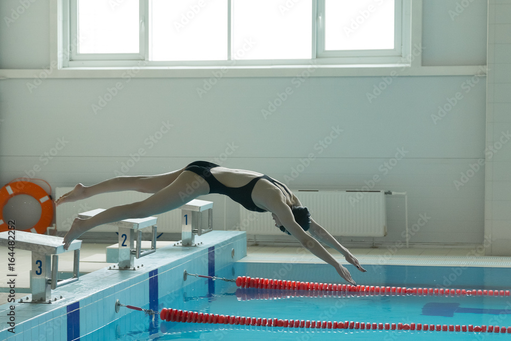 Young girl swimmer, that jumping and diving into indoor sport swimming ...