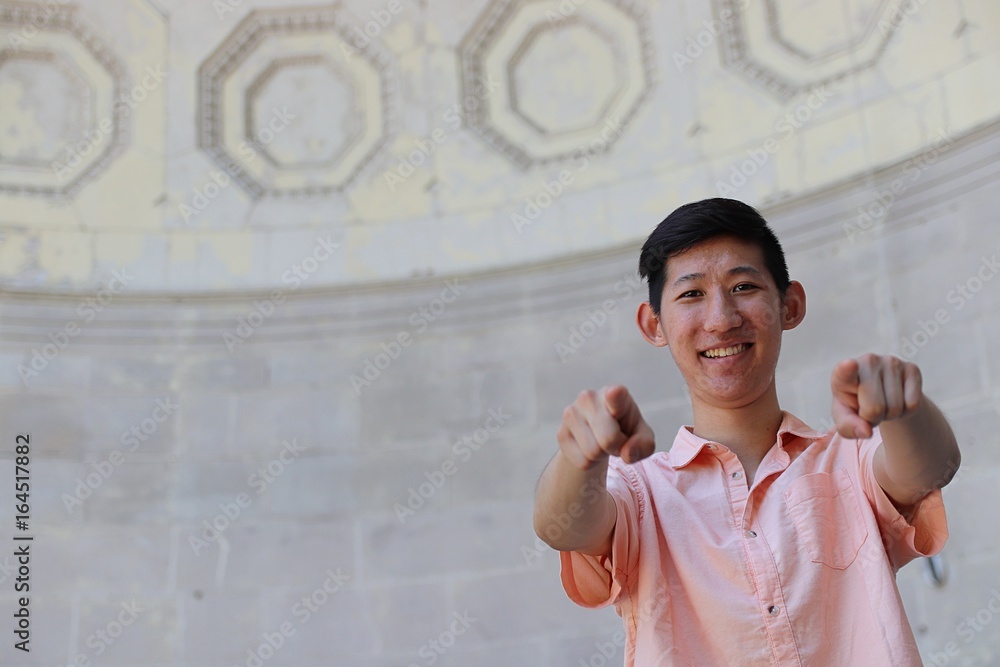 Young attractive asian man standing by concrete wall amphitheater ...