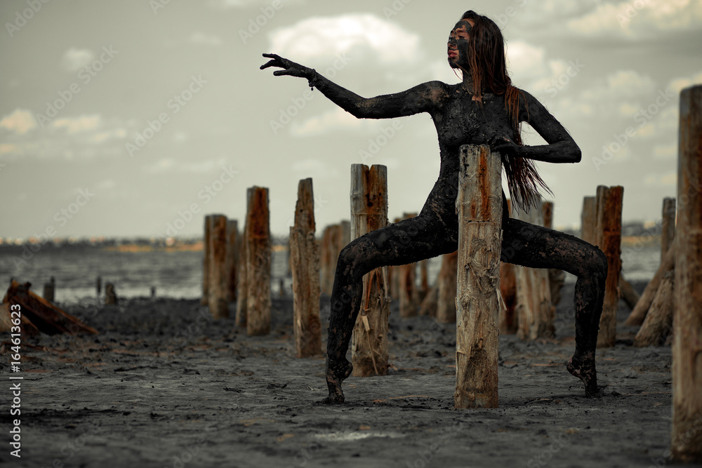 Young woman smeared with therapeutic mud and stands near wooden column ...