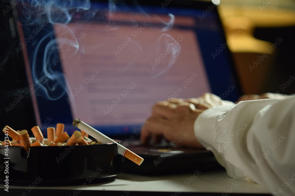 Man working on laptop computer with lit and smoking cigarette on an ...
