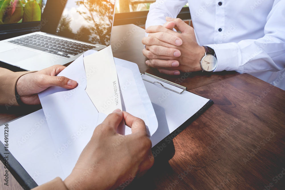 Hand of a businessman hands over a resignation letter on a wooden table ...