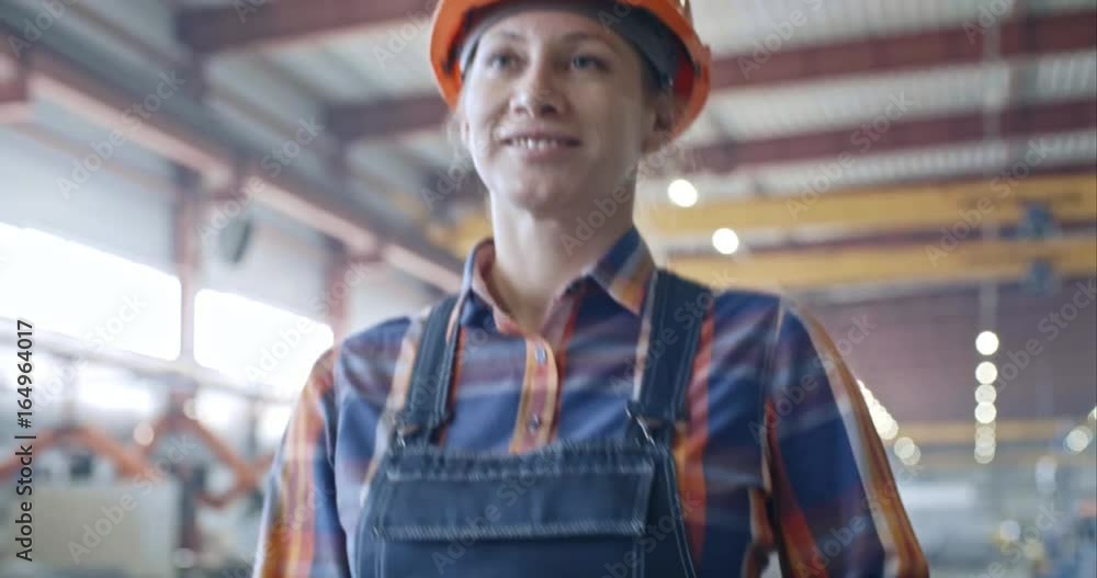 Tilt down of beautiful female factory worker walking through industrial ...