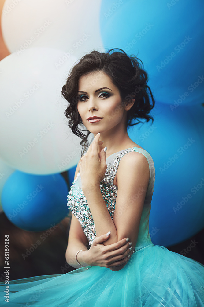 Girl in prom with helium air balloons. Portrait of a beautiful girl graduate in a blue dress ...